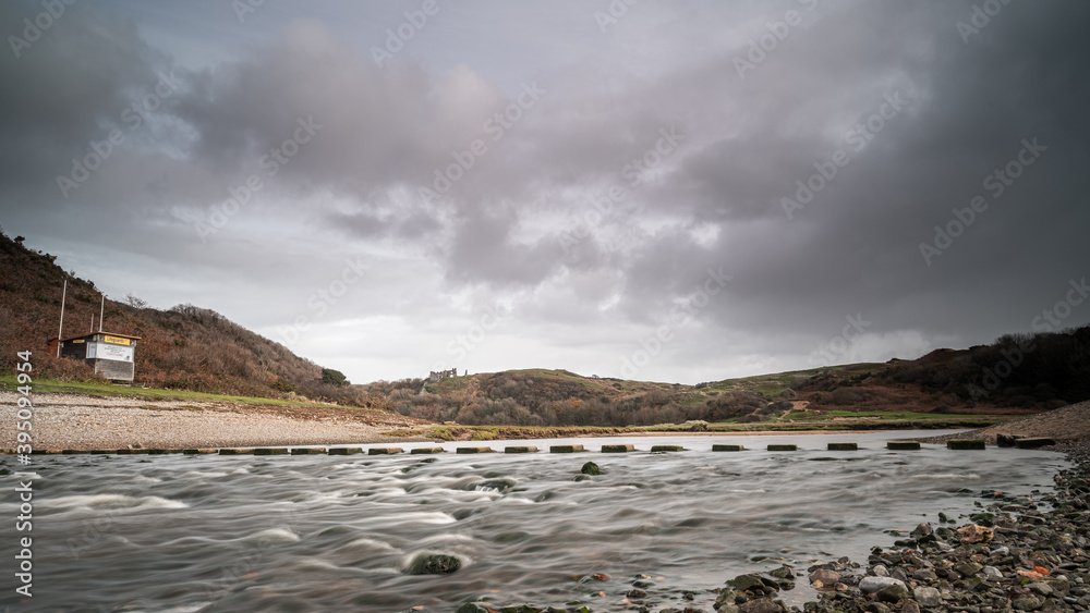 Stepping stones, crossing a river, with Pennard Castle, in the ...