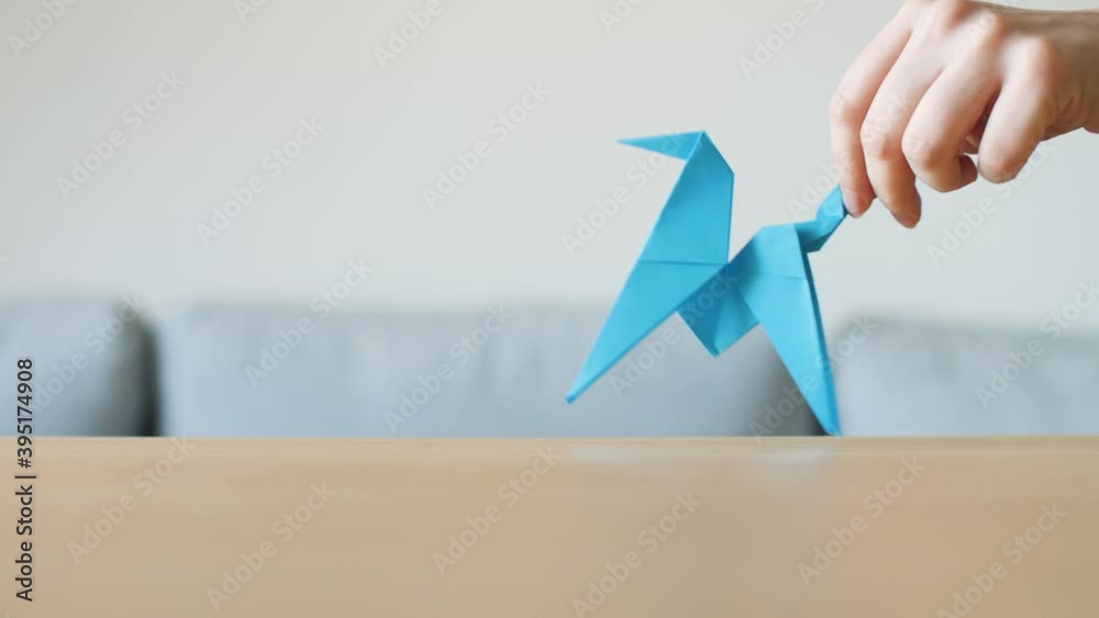 A hand moving a cute stylized blue handmade Origami Horse on a wooden ...