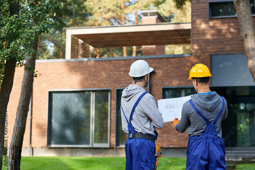 Making the best house. Rear view of two builders standing outdoors with ...