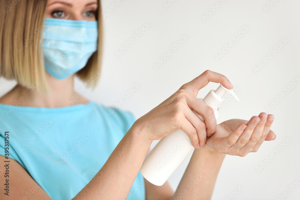Young woman using antiseptic gel and wearing prevention mask, close up ...