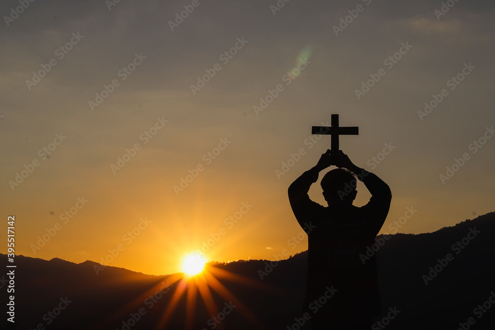Silhouette of human kneeling down praying and holding christian cross ...