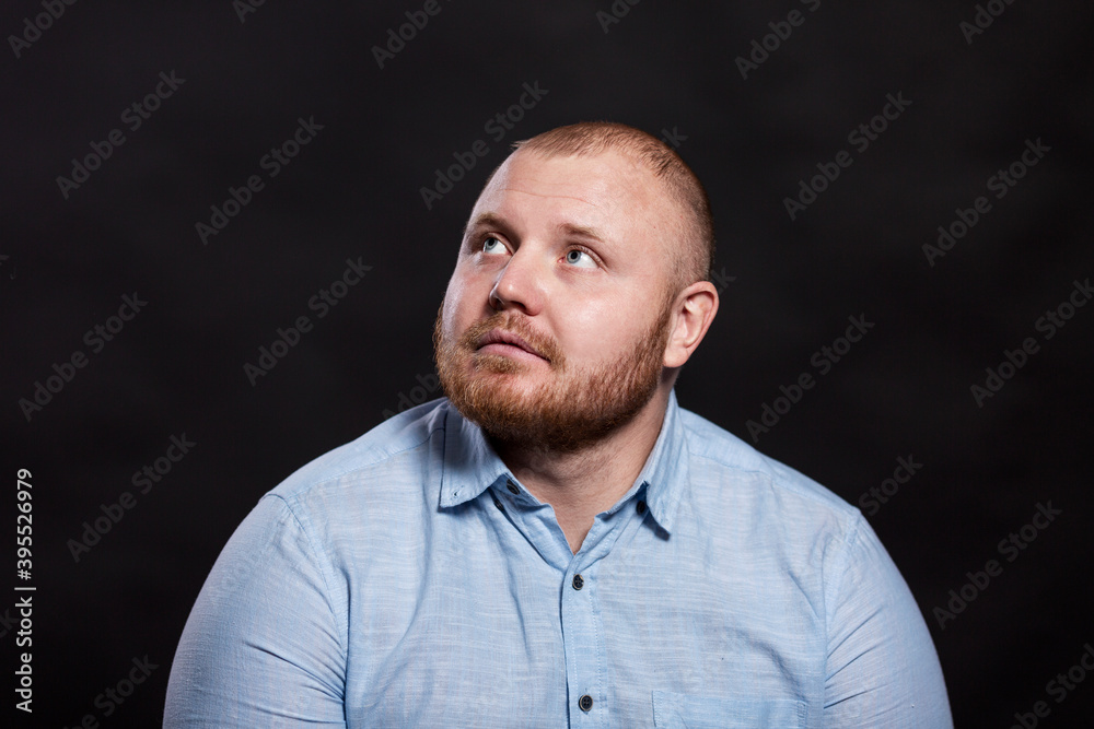 A fat man in a blue shirt sits and looks up. Black background. Stock ...