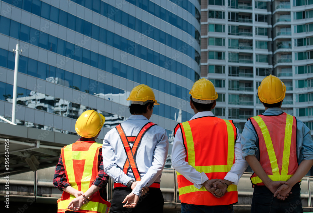 Backs of team successful men engineers with helmets looking on modern ...