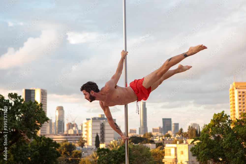 Muscular male pole dancer, holding a pose on a pole set outdoors. Tel ...