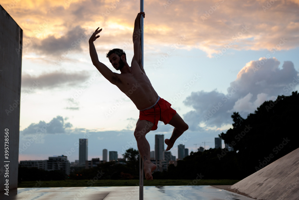 Muscular male pole dancer, holding a pose on a pole set outdoors ...