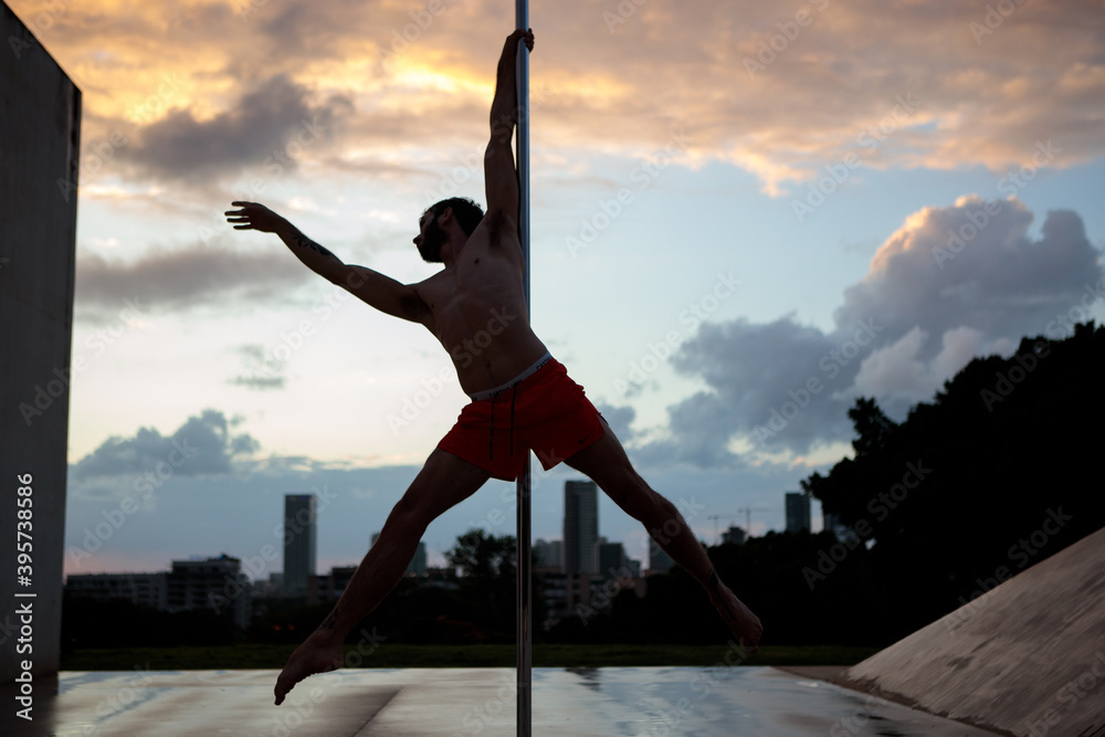 Foto de Muscular male pole dancer, holding a pose on a pole set ...