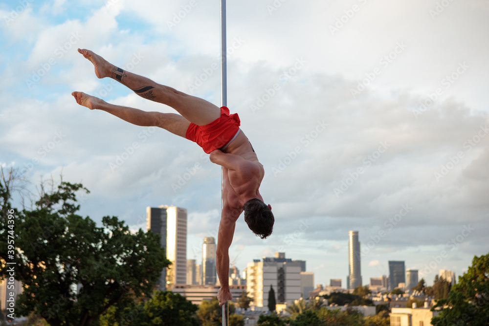 Muscular male pole dancer, holding a pose on a pole set outdoors. Tel ...