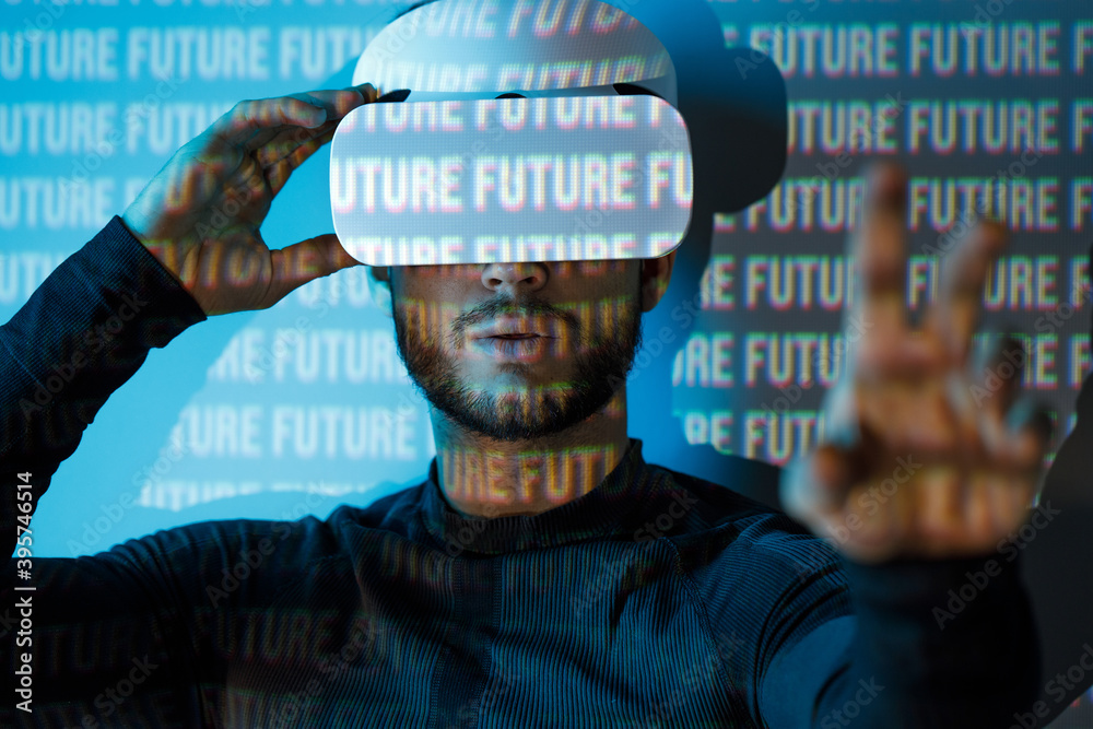 Young man in futuristic costume on blue neon light digital interface background. Guy using VR ...