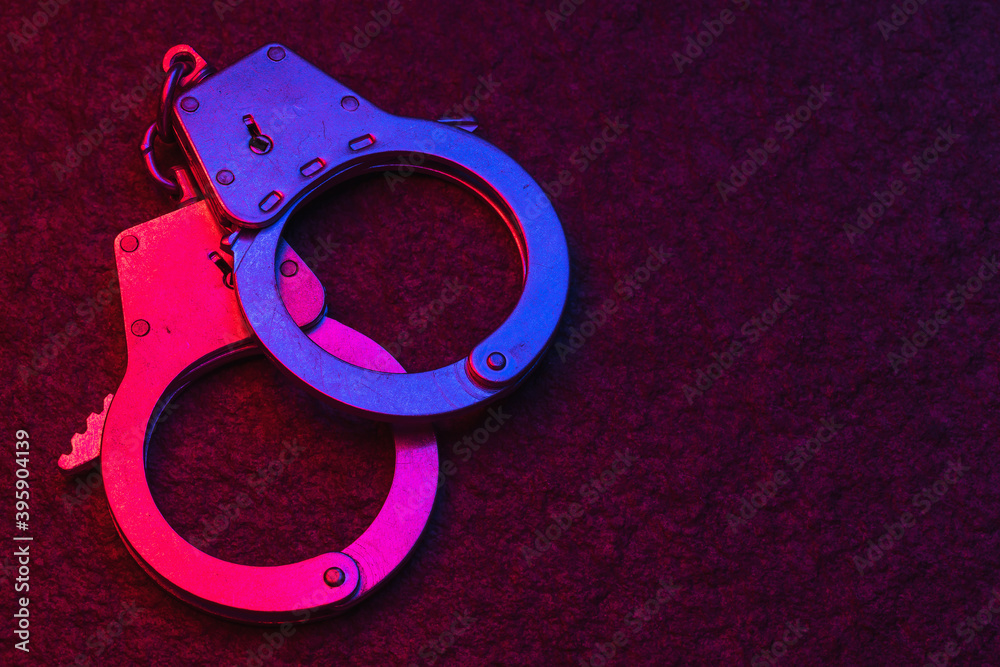 Handcuffs on dark background illuminated by flashing lights of police ...