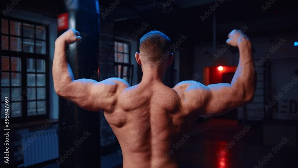 Strong man standing in the gym and showing his hands and back muscles ...