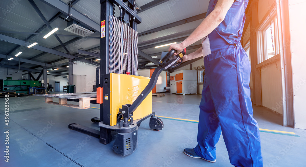 A worker in a warehouse uses a hand pallet stacker to transport pallets ...