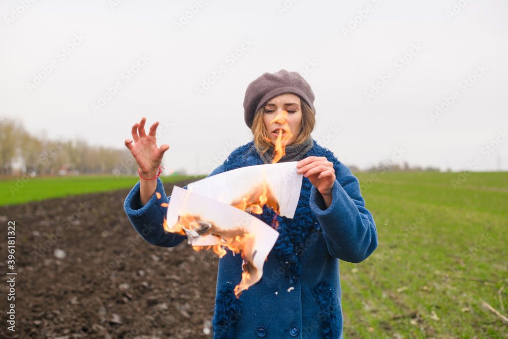 Desperate angry girl in blue coat hold burning paper with fire at open ...