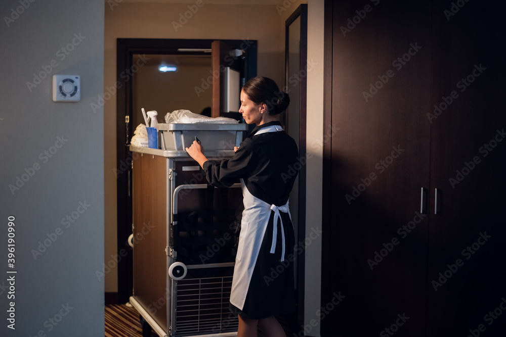 Hotel service. A female housekeeping worker with a trolley entering a ...