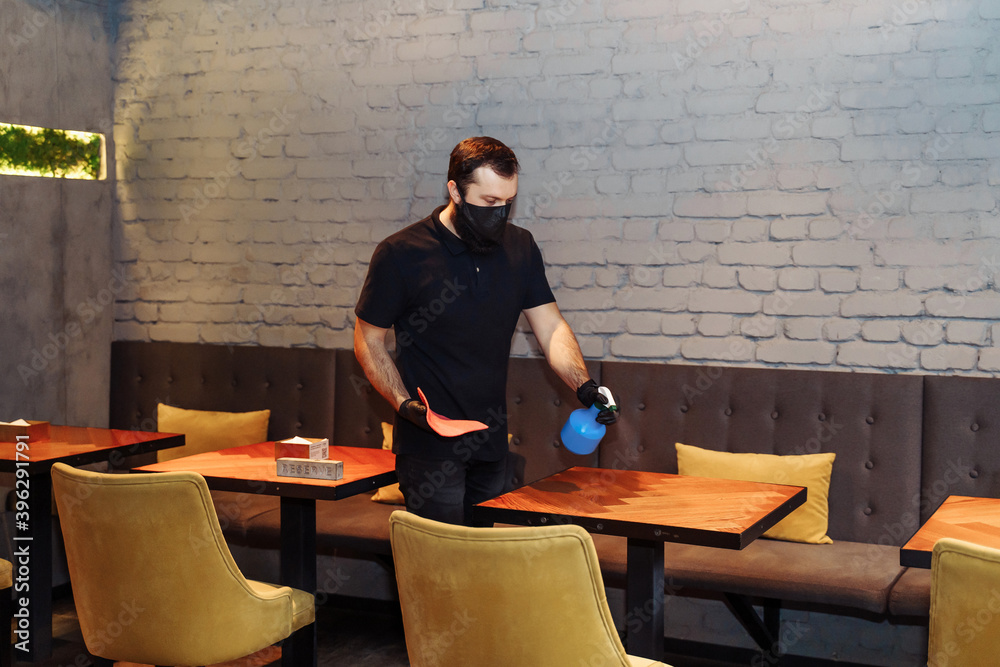 Waiter wearing protective face mask and gloves while disinfecting ...