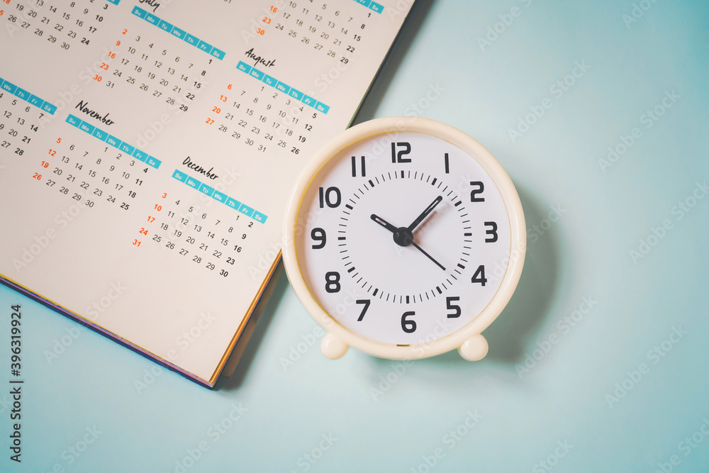 white analog clock on yearly calendar and green background , top view ...