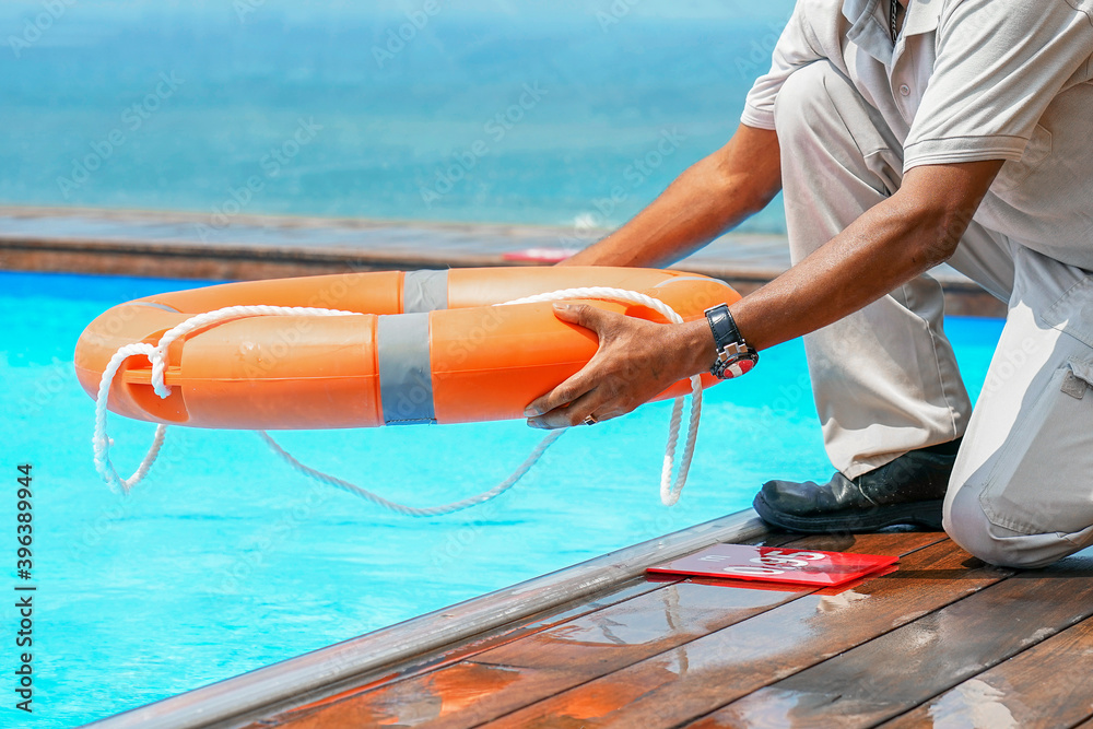African man rescuer with lifebuoy in pool. African hotel worker throws ...