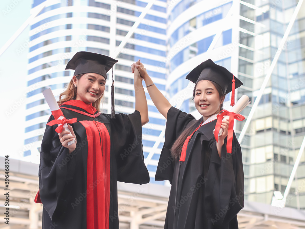 happy graduated women in graduation gowns, holding diplomas, smiling ...