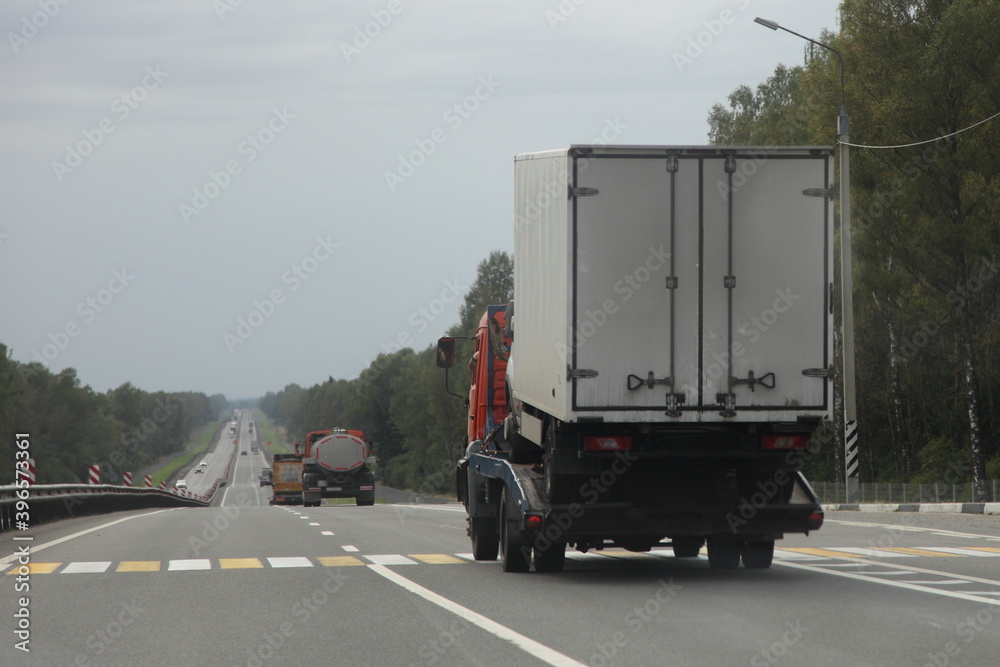 Car carrier truck transports van truck on suburban motorway, rear side ...