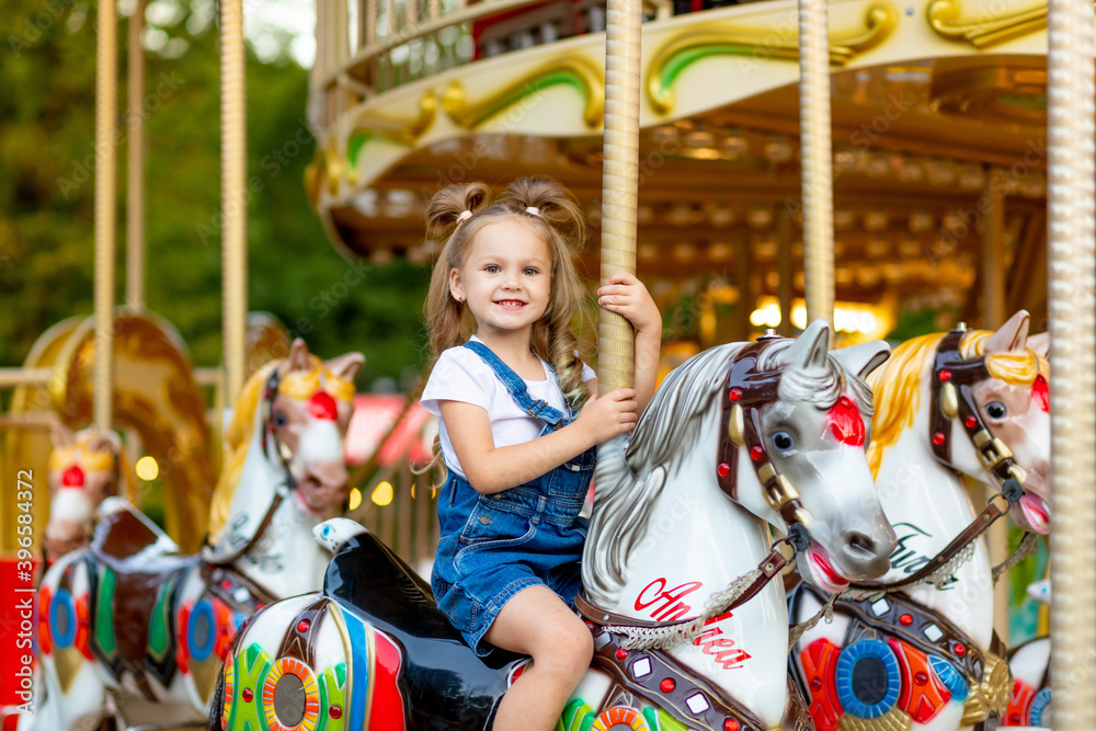 happy baby girl rides a carousel on a horse in an amusement Park in ...