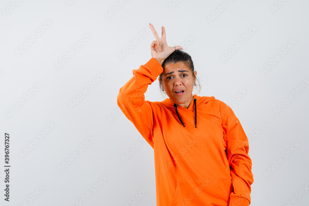 lady showing I love you gesture over head in orange hoodie and looking ...