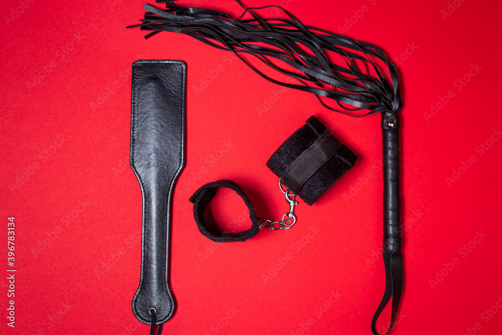 BDSM accessories on a red background. A leather paddle, padded ...