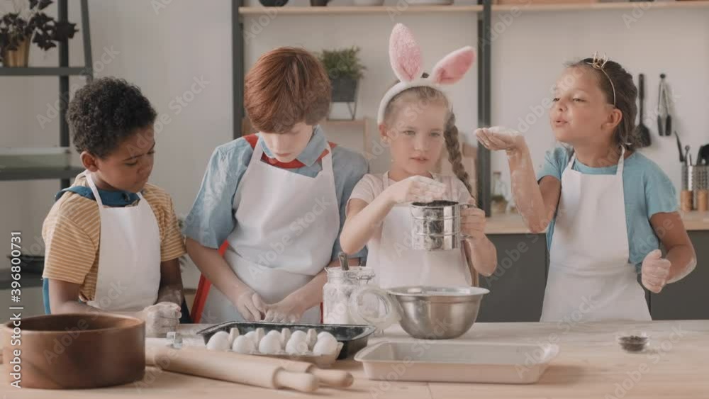 Diverse school children having fun, making mess in kitchen, standing at ...