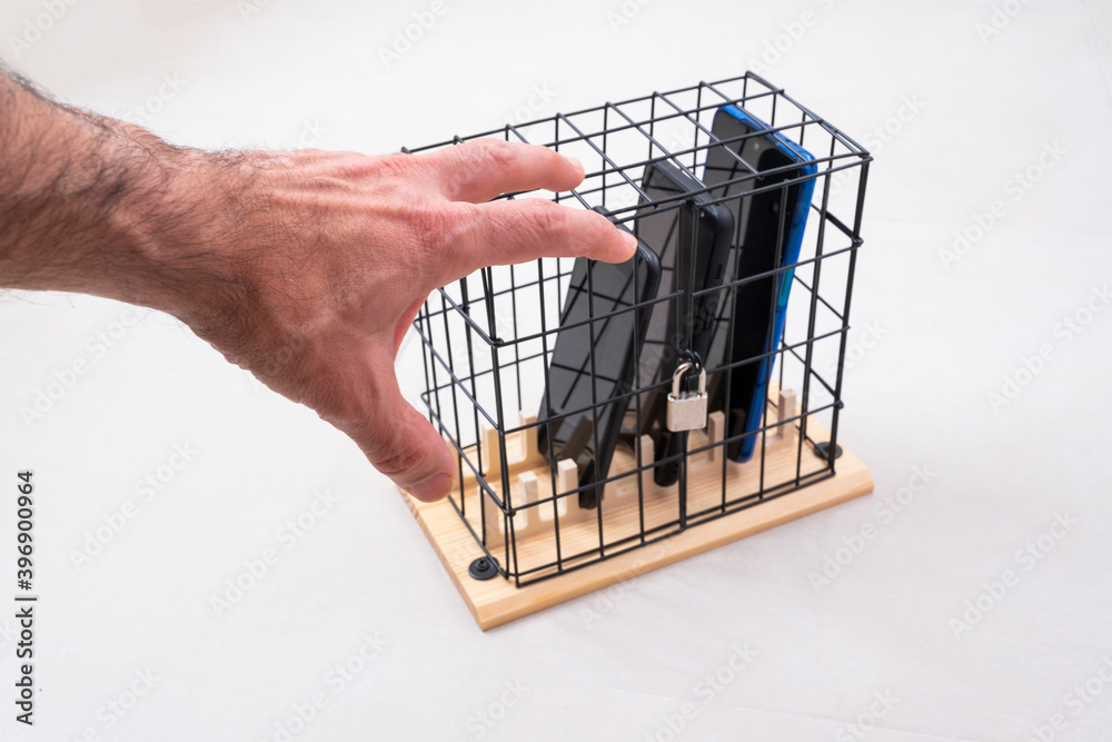 hand trying to catch three mobile phones locked in a cage with a ...