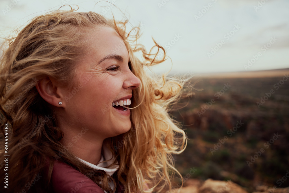 Closeup of a laughing young woman enjoying windy breeze touching face ...