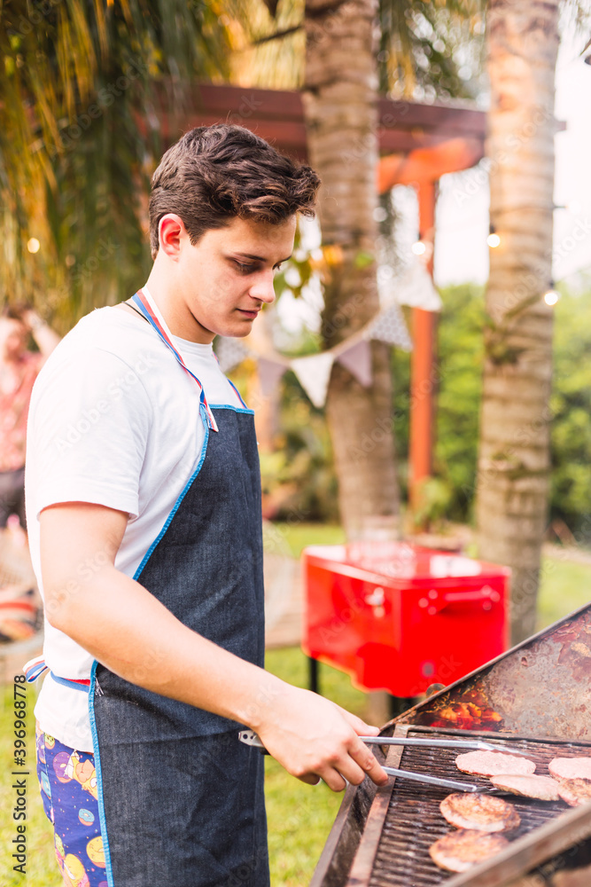 Young man cooking hamburgers on the outdoor grill in the sun - Portrait ...