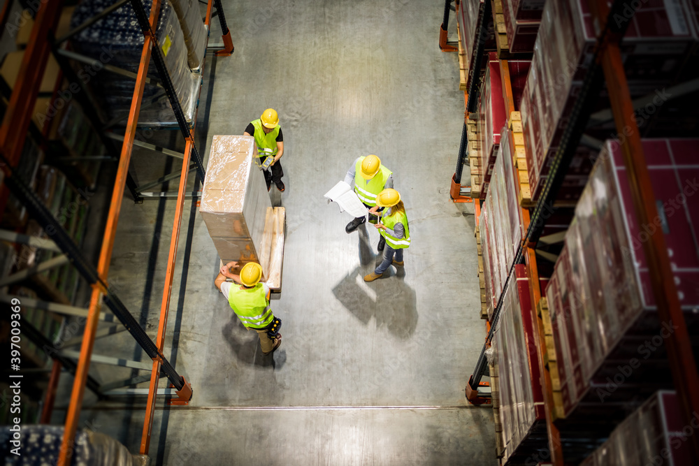 Warehouse workers at work between rows of tall shelves full of packed ...