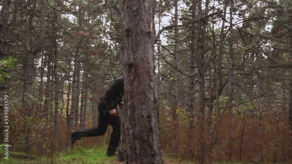 athlete in black clothes, hat, runs quickly through dark forest ...