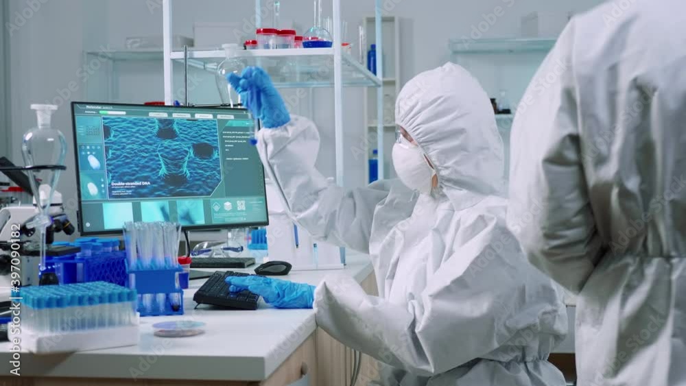 Scientist nurse in ppe suit taking notes on computer looking at test ...