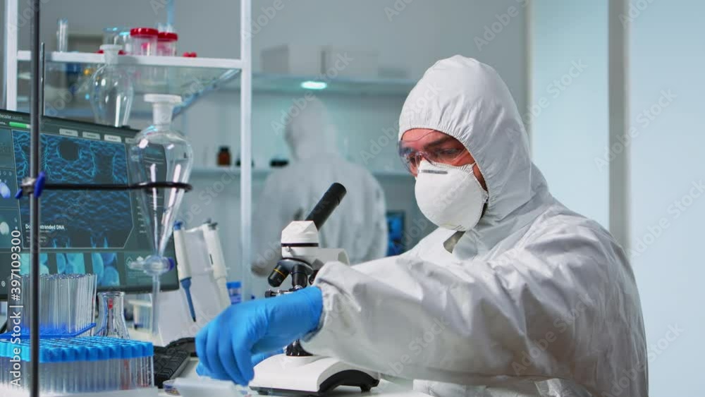Scientist in ppe suit placing a slide on specimen stage of a laboratory ...