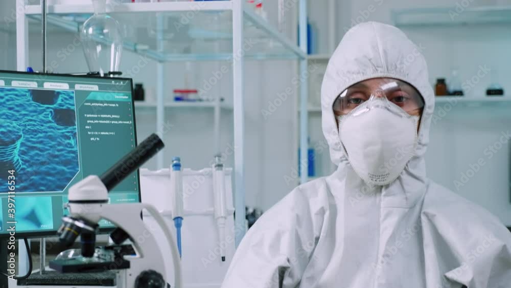 Microbiologist sitting in laboratory wearing ppe suit looking at camera ...