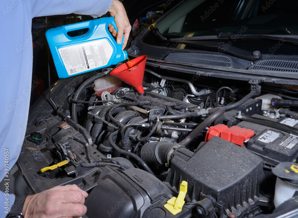 Pouring motor oil into a car engine using a funnel as part of ...