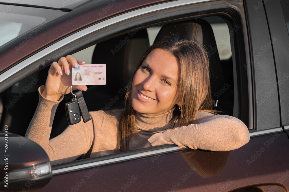 Attractive smiling young woman proudly showing her driving license out ...