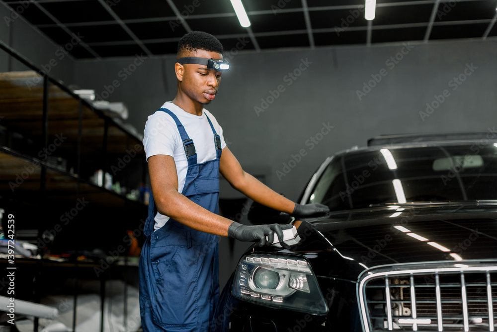 African male auto service worker, coating luxury black car with ...