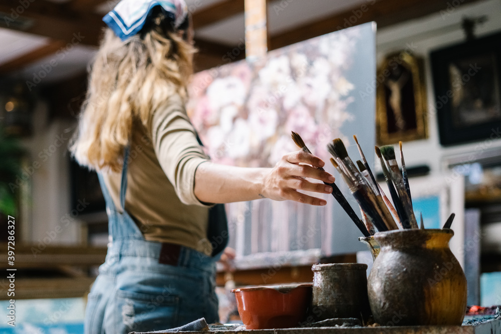 Low angle side view of female artist taking paintbrush from pot with ...