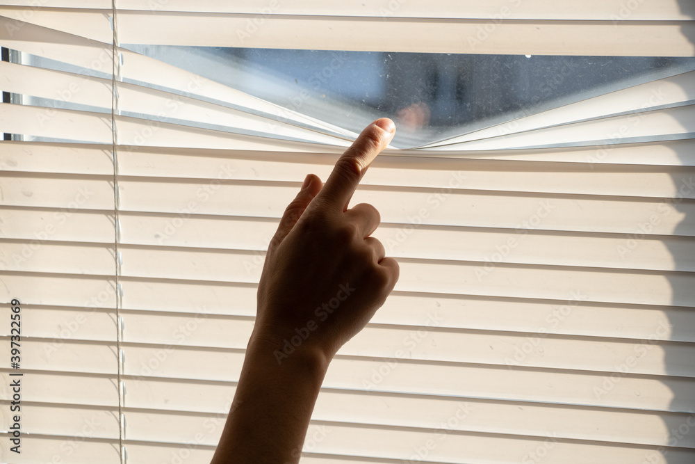 finger on the blinds on the window of the house, look out the window ...