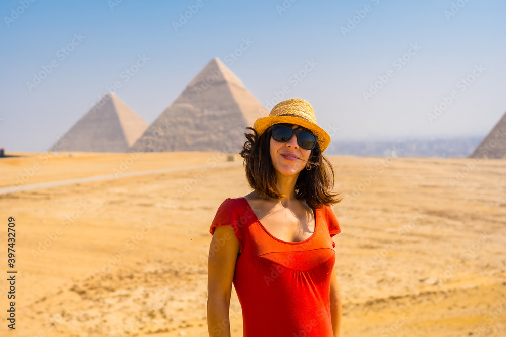Portrait of a young tourist in red dress enjoying the pyramids of Giza ...