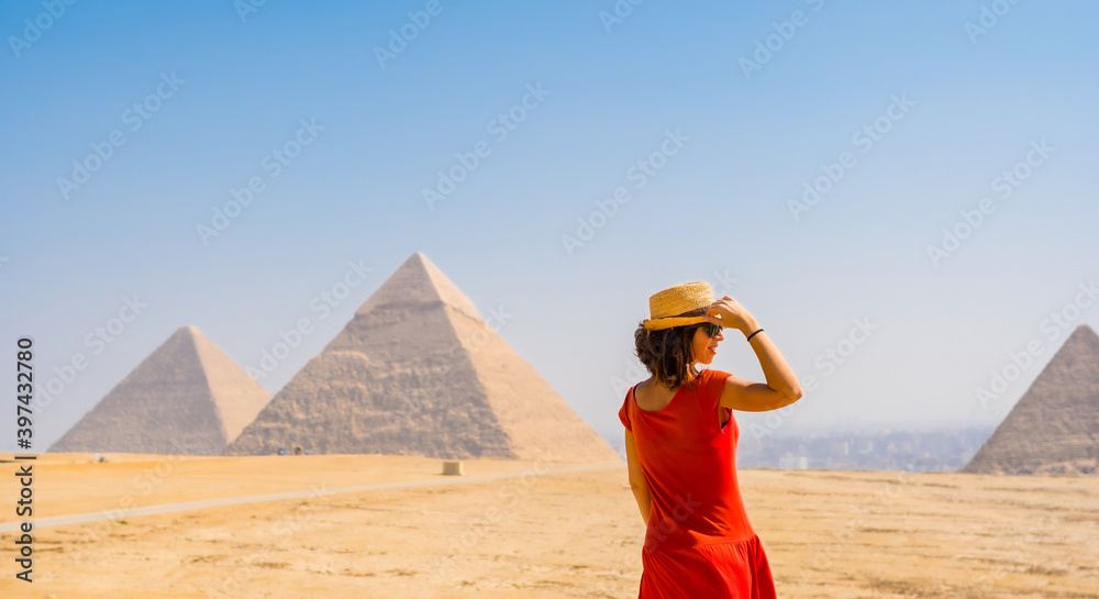 A tourist girl in a red dress looking at the Pyramids of Giza, the ...