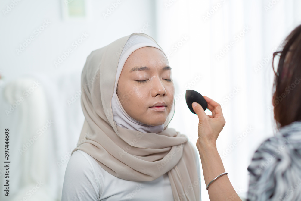 Makeup artist applies brush on cheeks with young muslim woman in hijab ...