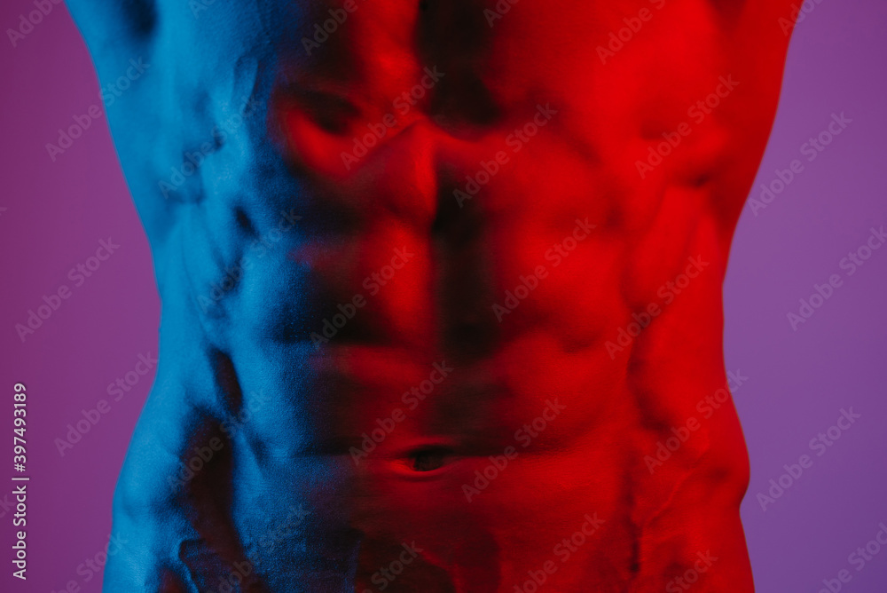 A front photo of the abs of a bodybuilder under blue and red lights. An ...
