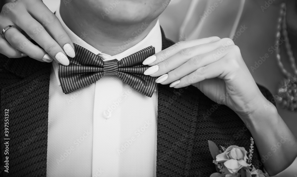 Bride adjusting the bowtie of the groom. Woman's hands touch the tie of ...