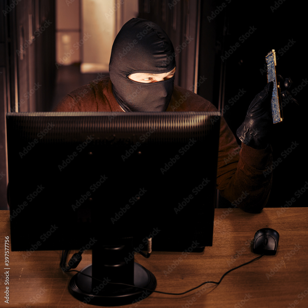 Hacker in black balaclava with a printed circuit board from the device ...
