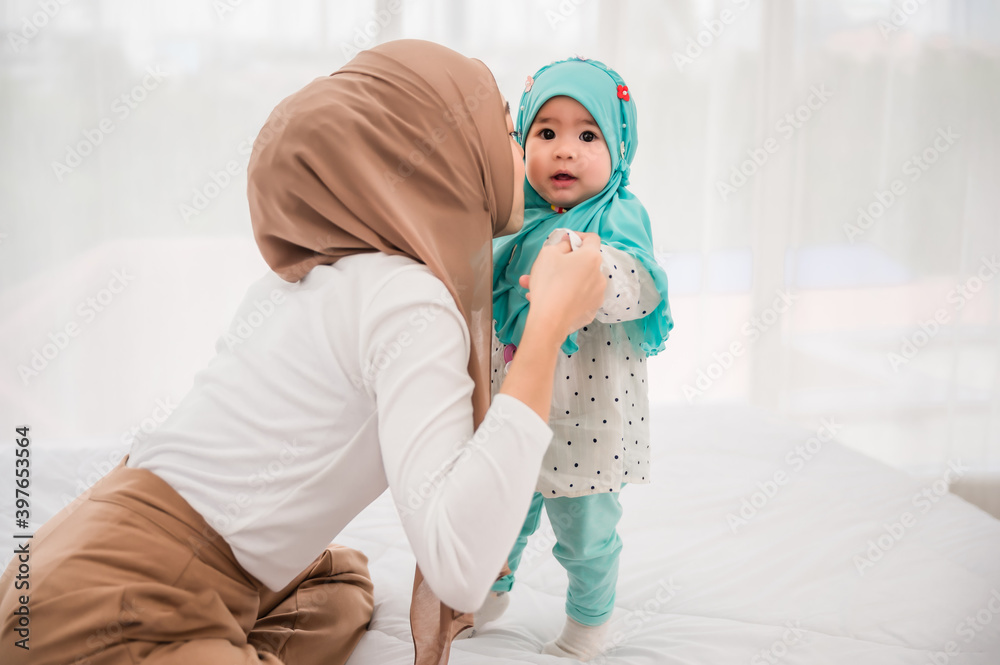 Happy muslim mother and adorable little baby daughter in hijab on bed ...