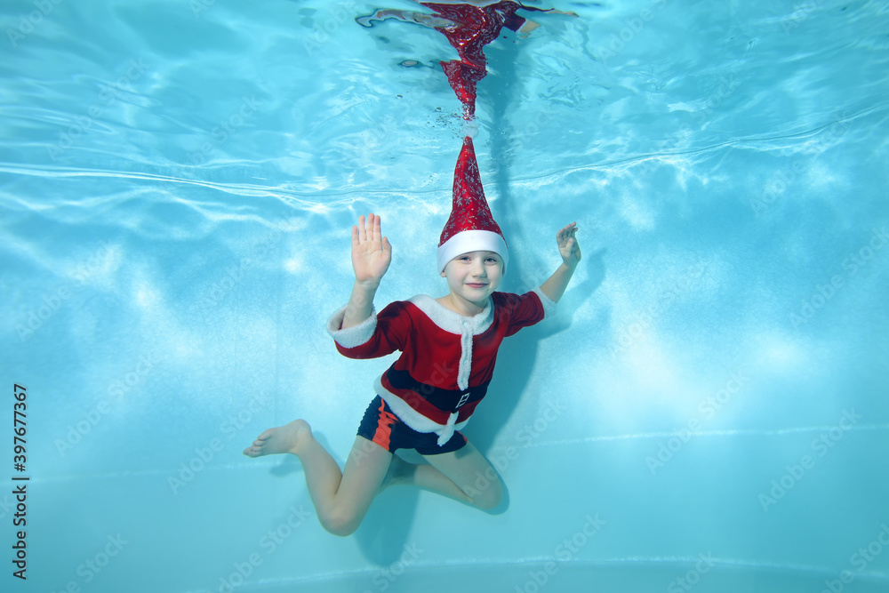 Smiling underwater boy in Santa Claus costume in the pool. Baby learns ...