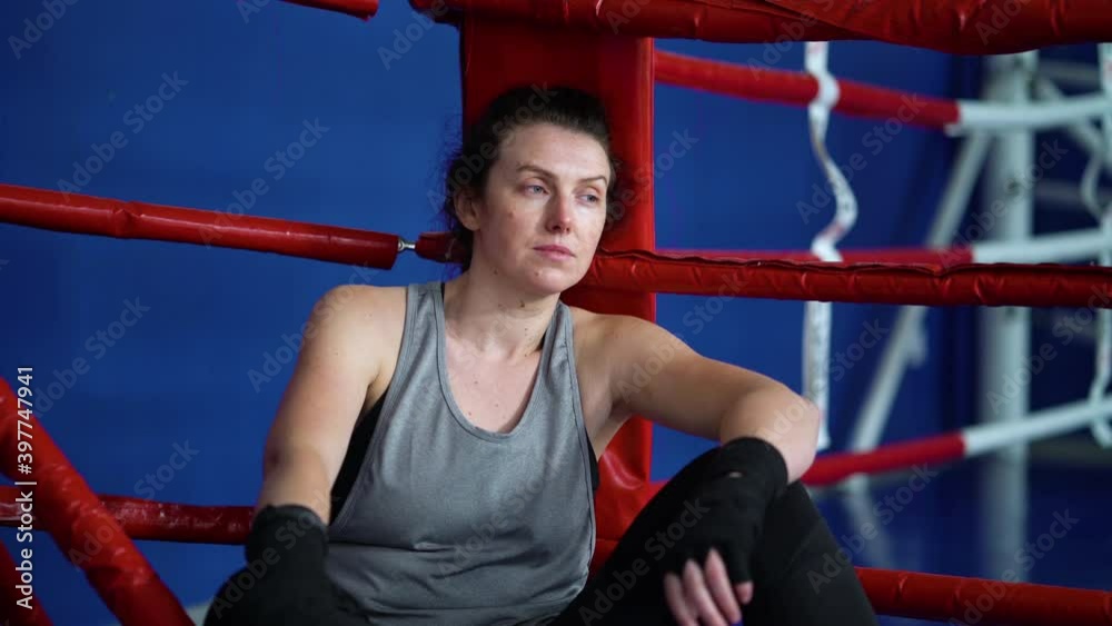 Woman in sportswear and bandages on wrists relaxing on floor in corner ...