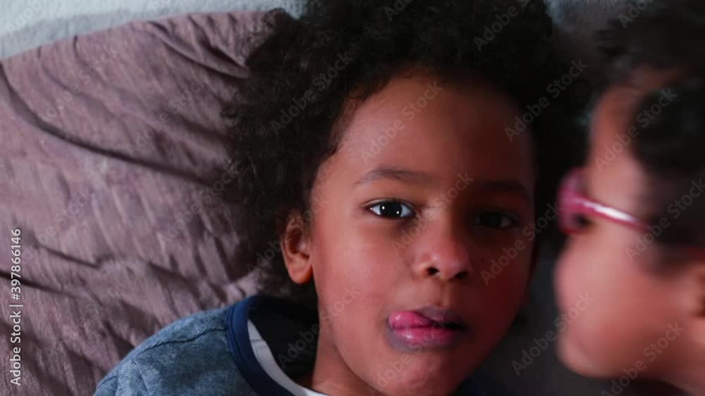 Two black children are fooling around lying on bed. The sister kisses ...