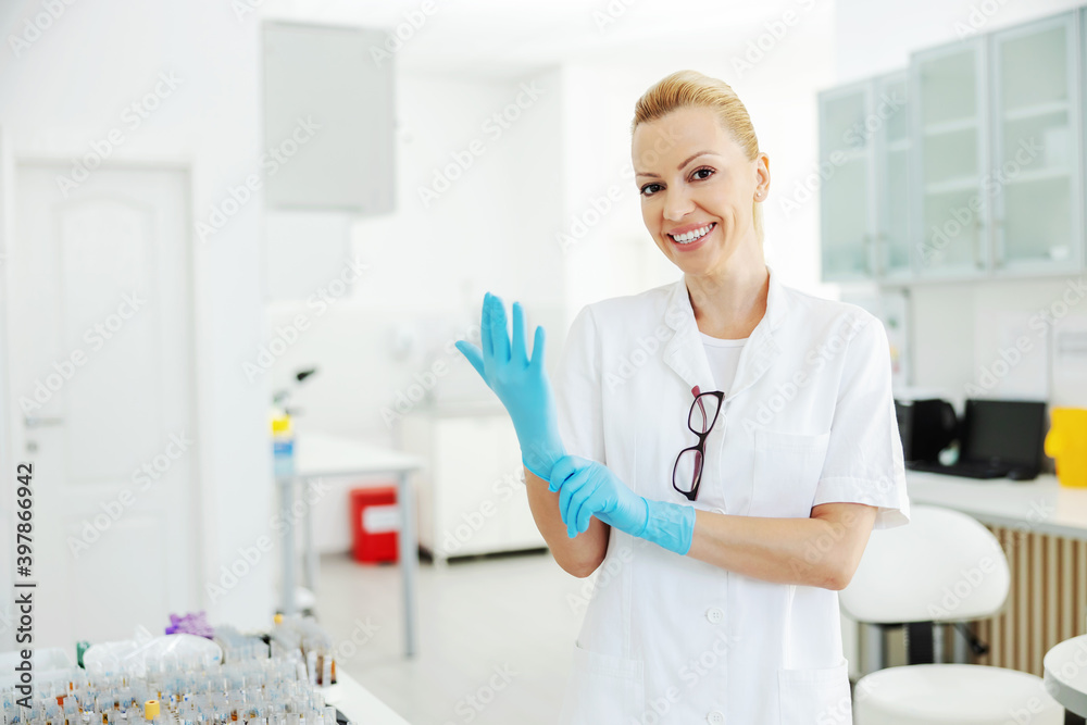 Middle aged attractive lab assistant in sterile white uniform standing ...